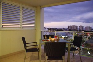 Varanda com mesa posta para dois, cadeiras e vista para a cidade ao entardecer.