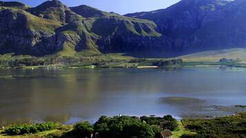 Um lago rodeado por montanhas, com um pequeno povoado e edifícios com telhados de palha perto da margem.