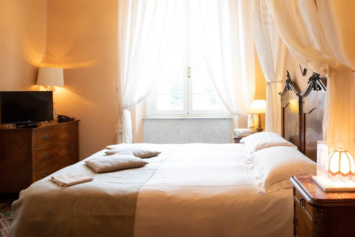 Cama bem arrumada com almofadas, televisão em cômoda de madeira e abajur.