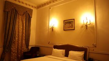 Quarto de hotel com cama, mesa de cabeceira, cadeira e luminária fixada na parede.