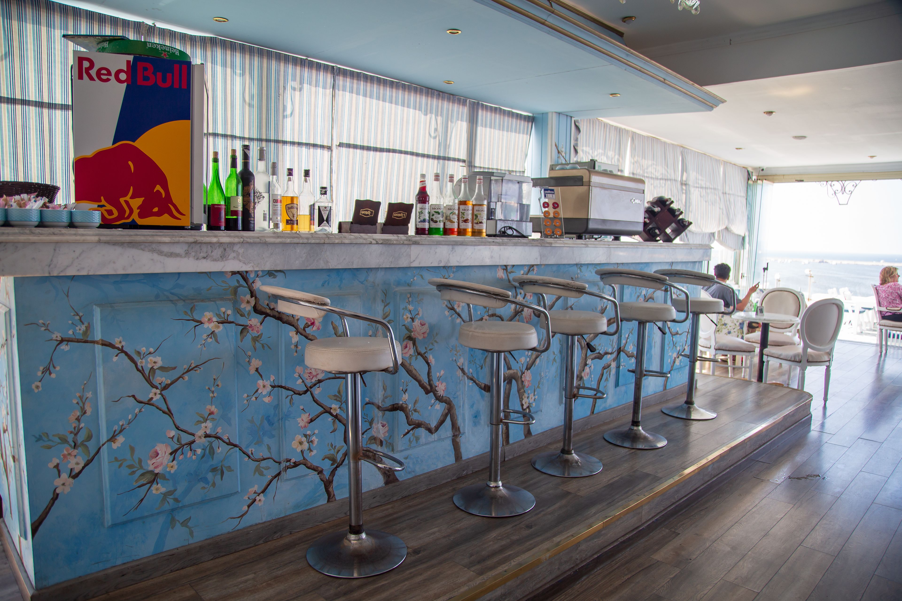 Uma área de bar com um refrigerador Red Bull, várias garrafas de bebidas alcoólicas e banquetas.