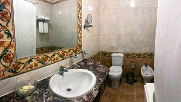 Uma casa de banho com lavatório de mármore, sanita, bidé e espelho com moldura de azulejos decorativos.