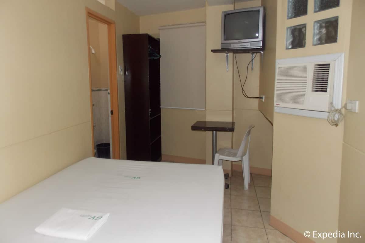 Quarto de hotel pequeno com cama, escrivaninha, televisão e guarda-roupa.