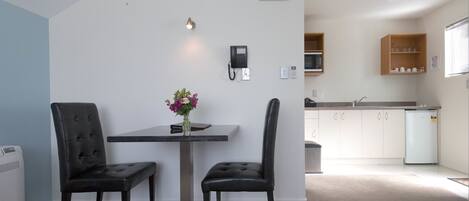 Uma cozinha moderna com armários brancos, micro-ondas e geladeira. Há uma área de jantar com uma mesa e duas cadeiras, e um vaso com flores sobre a mesa.