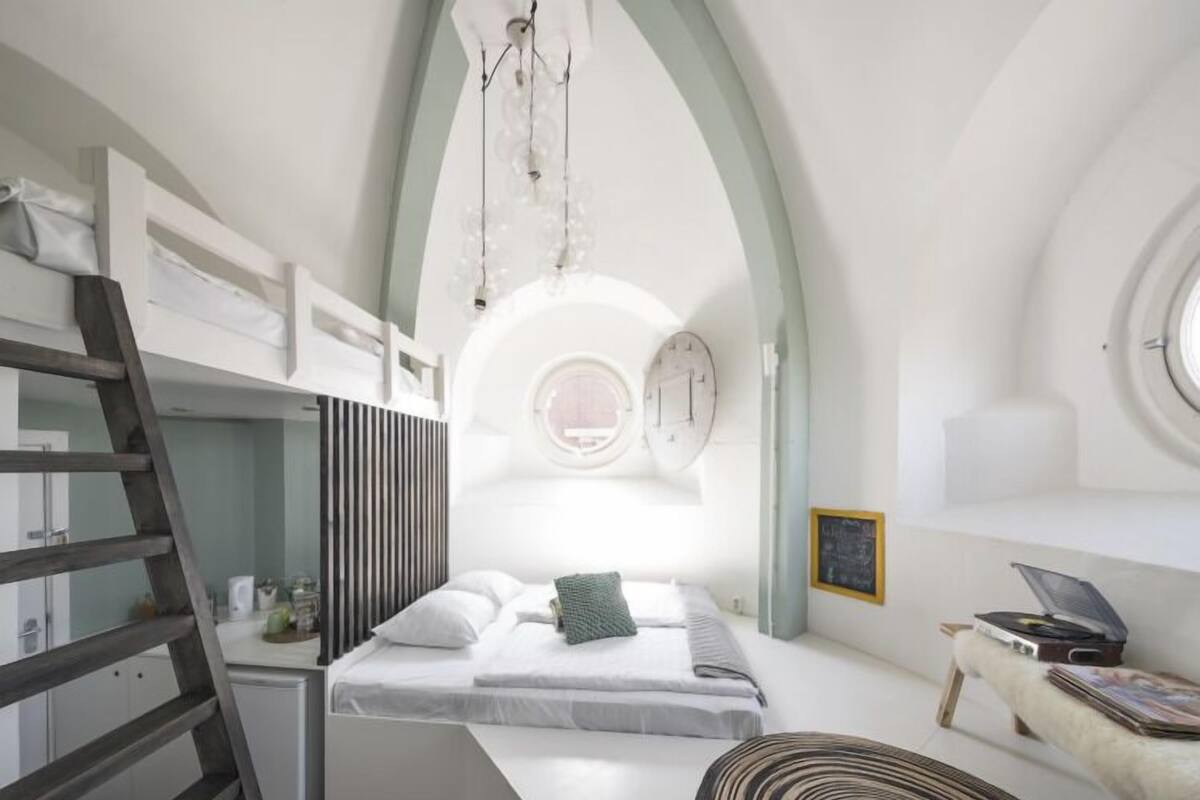 Quarto moderno com cama beliche, escrivaninha e janela redonda.