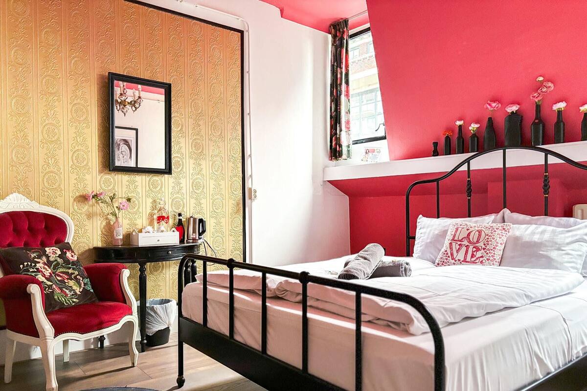 Um quarto com cama, poltrona, mesa e parede com papel de parede estampado.