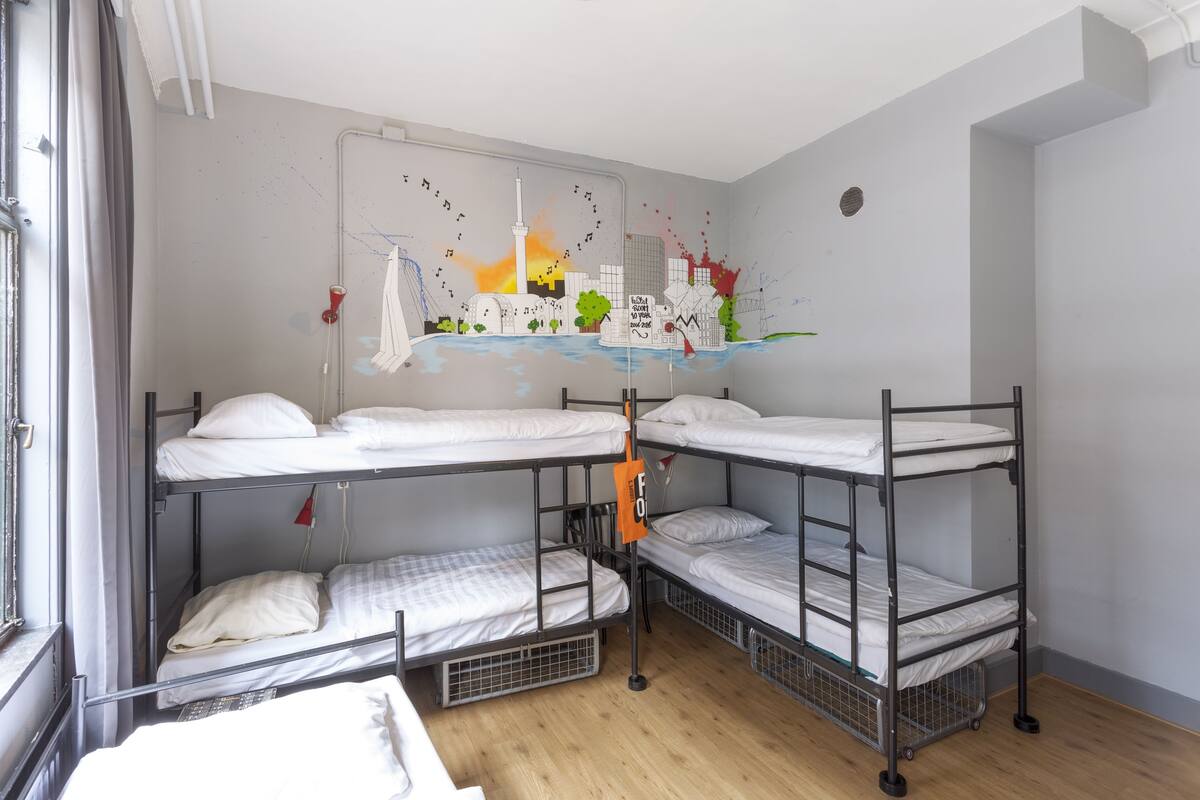 Quarto de dormitório com beliches, um mural com vista urbana na parede e uma janela com cortinas.