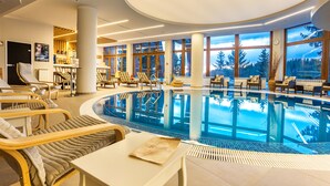Uma área interna de piscina moderna com espreguiçadeiras e vista para uma floresta através de grandes janelas.