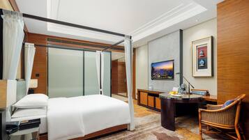 Quarto de hotel com cama, escrivaninha, cadeira, televisão e quadro na parede.