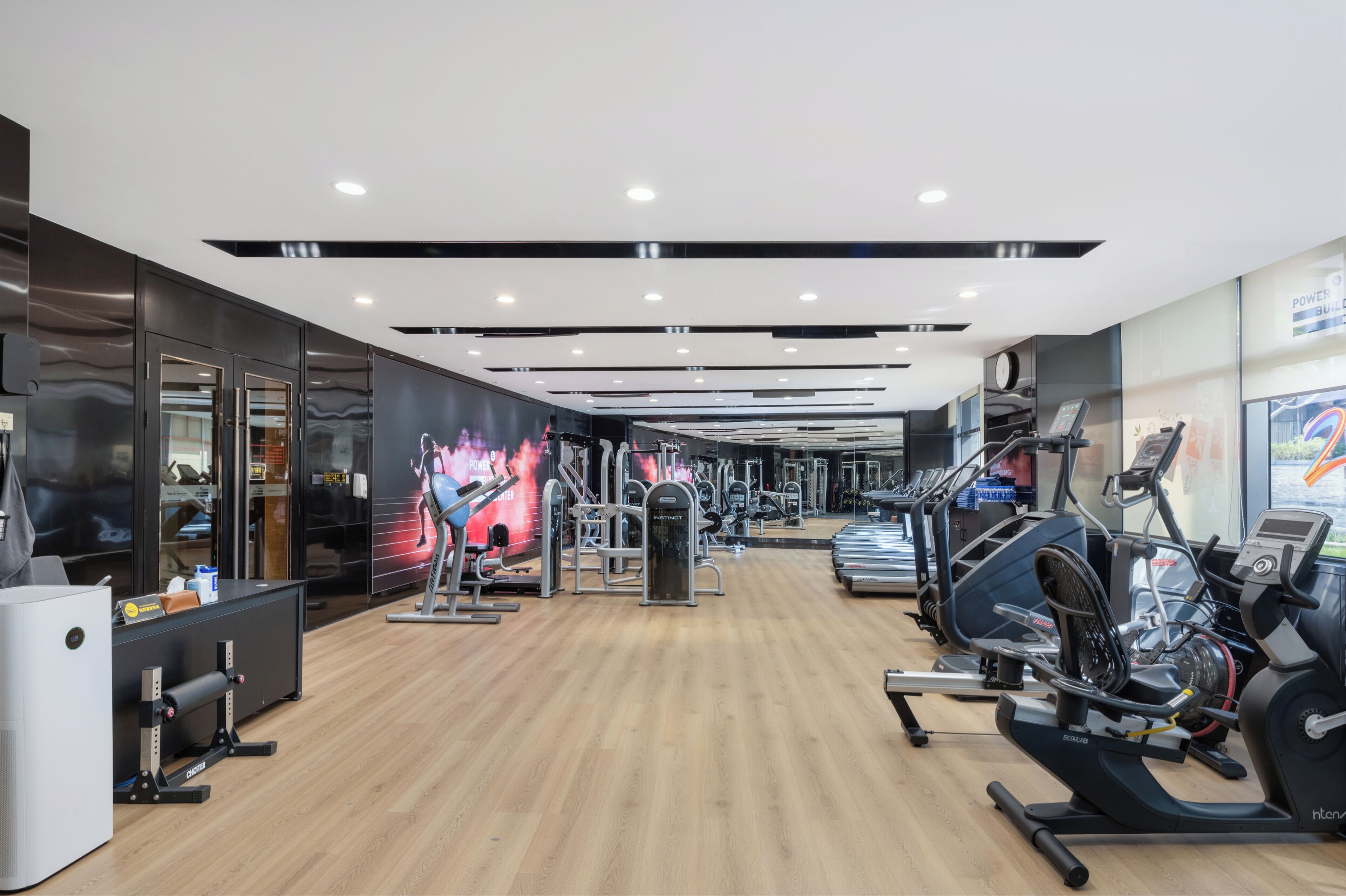 Uma academia moderna com diversos equipamentos de exercícios, piso de madeira e um grande espelho em uma parede.