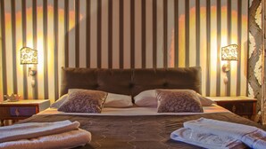 Quarto de hotel com uma cama grande, duas mesas de cabeceira e duas luminárias fixadas na parede.