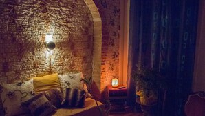 Um quarto aconchegante com parede de pedra, um sofá com almofadas estampadas, uma mesa com luminária de sal e uma planta em vaso.