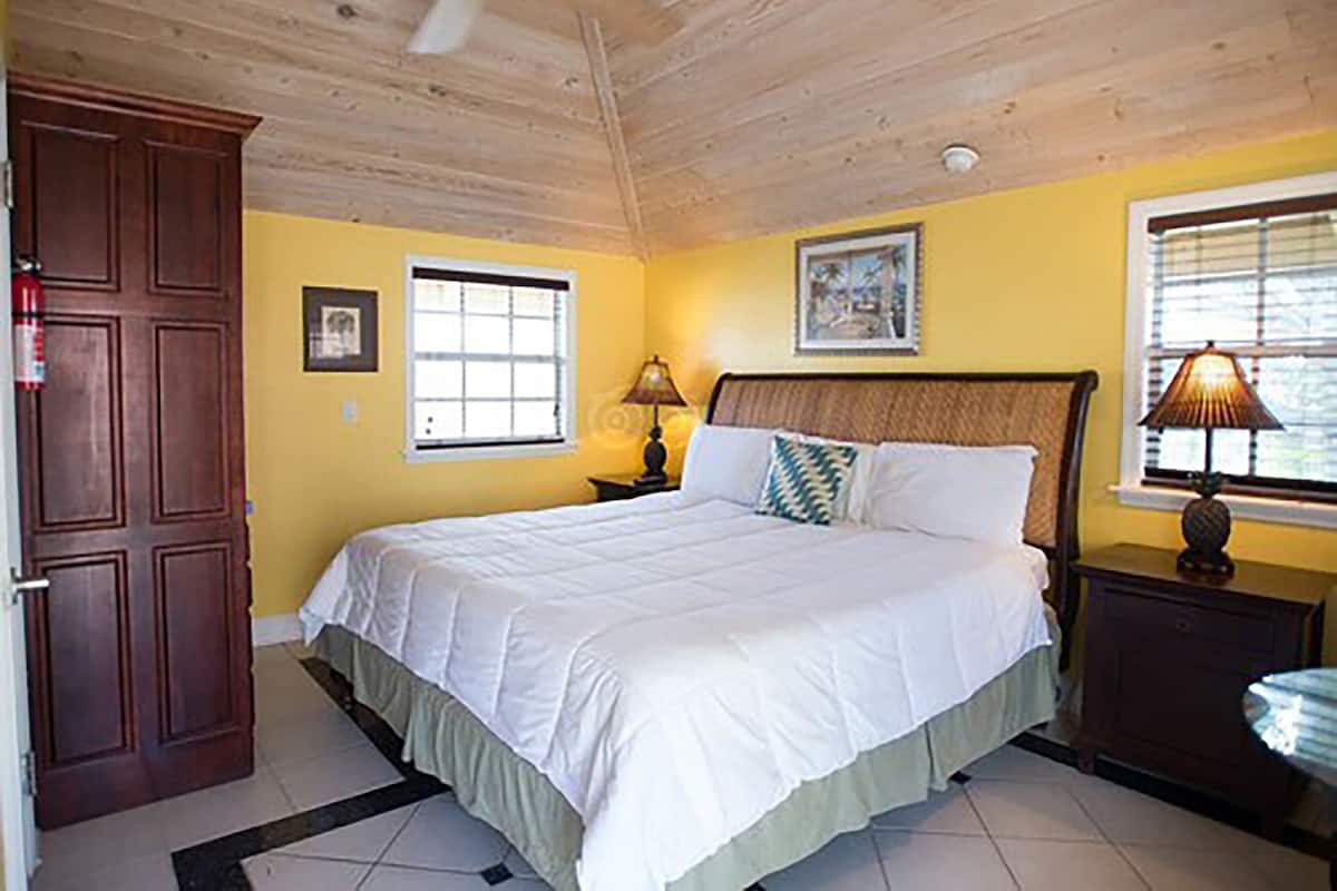 Um quarto com uma cama grande, teto de madeira, paredes amarelas, uma janela e uma porta.