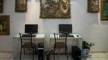 Quarto com duas mesas, cada uma com um computador e uma cadeira. Quadros emoldurados na parede.
