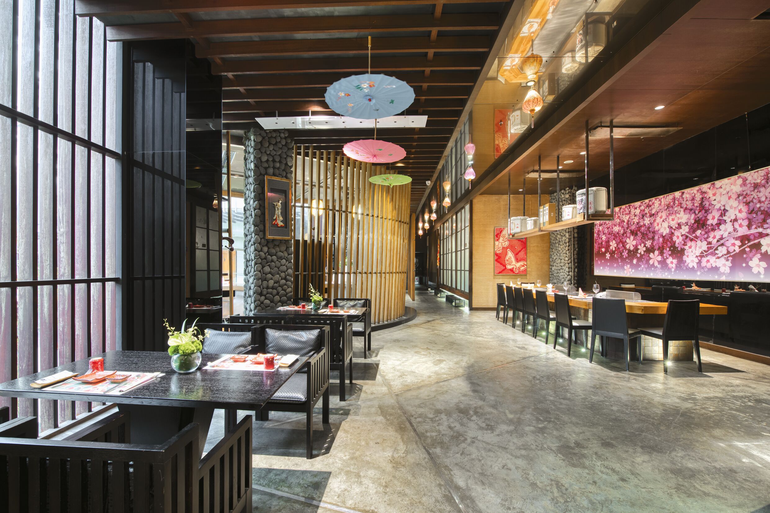 Interior de restaurante moderno com mobiliário de madeira, bar de sushi e guarda-sóis decorativos.