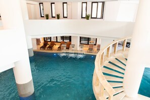 Piscina interior com vários níveis, escadaria, área de estar e grandes janelas.