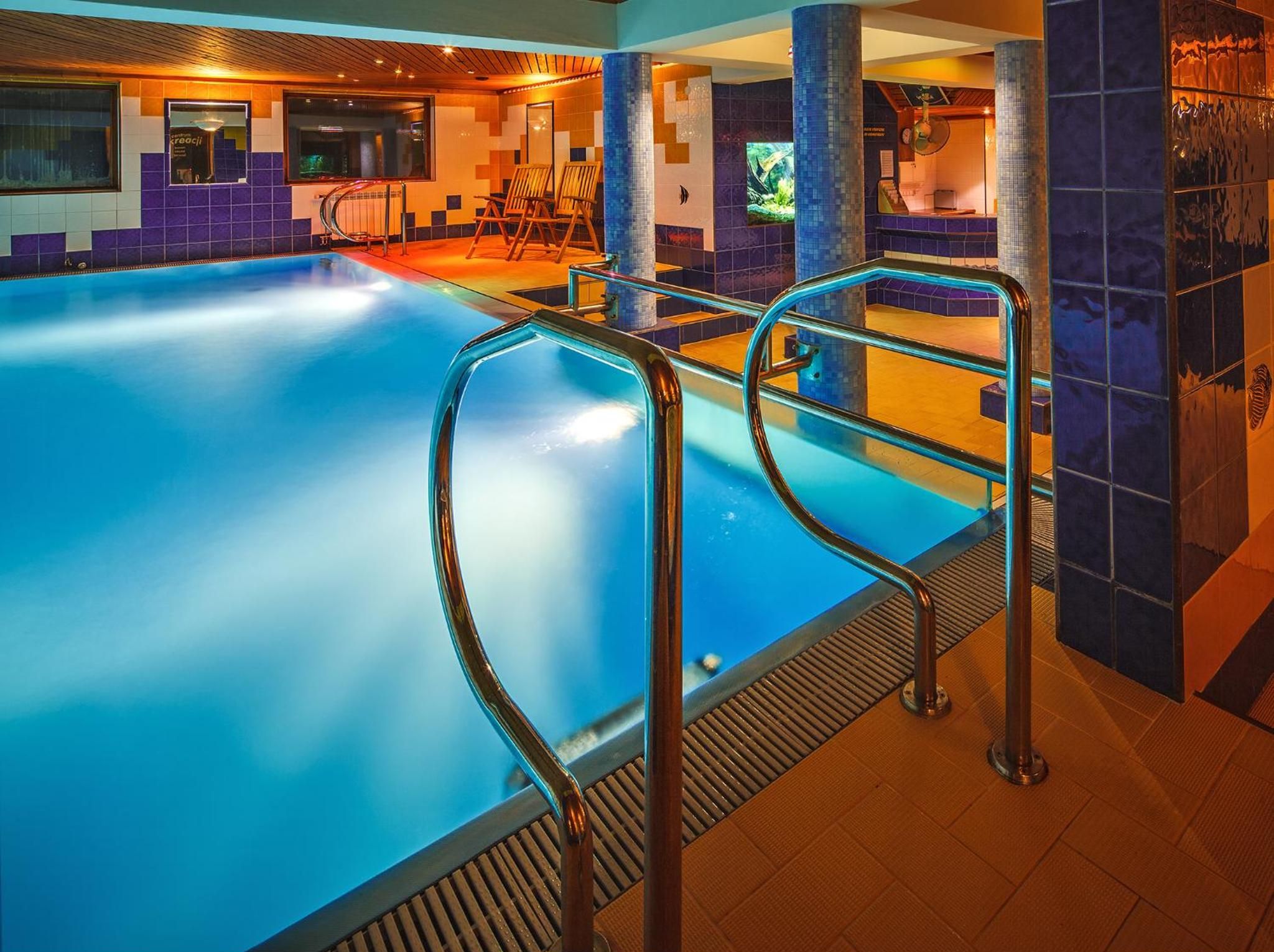 Piscina com guarda-corpo de metal, rodeada por paredes azulejadas e teto de madeira.