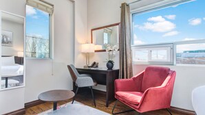 Quarto de hotel com escrivaninha, cadeira e uma janela grande com vista para a cidade.