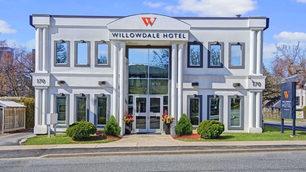 Exterior do Hotel Willowdale, com fachada simétrica, entrada central, janelas amplas e o logotipo 'W' em destaque acima da entrada.