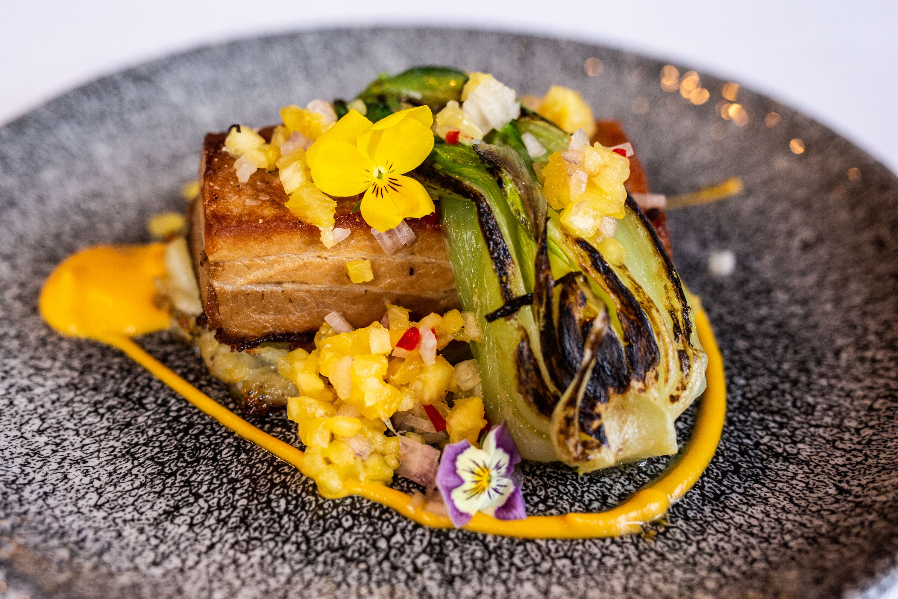 Prato com legumes grelhados, uma flor e molho sobre uma superfície texturizada.