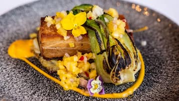 Prato com legumes grelhados, uma flor e molho sobre uma superfície texturizada.