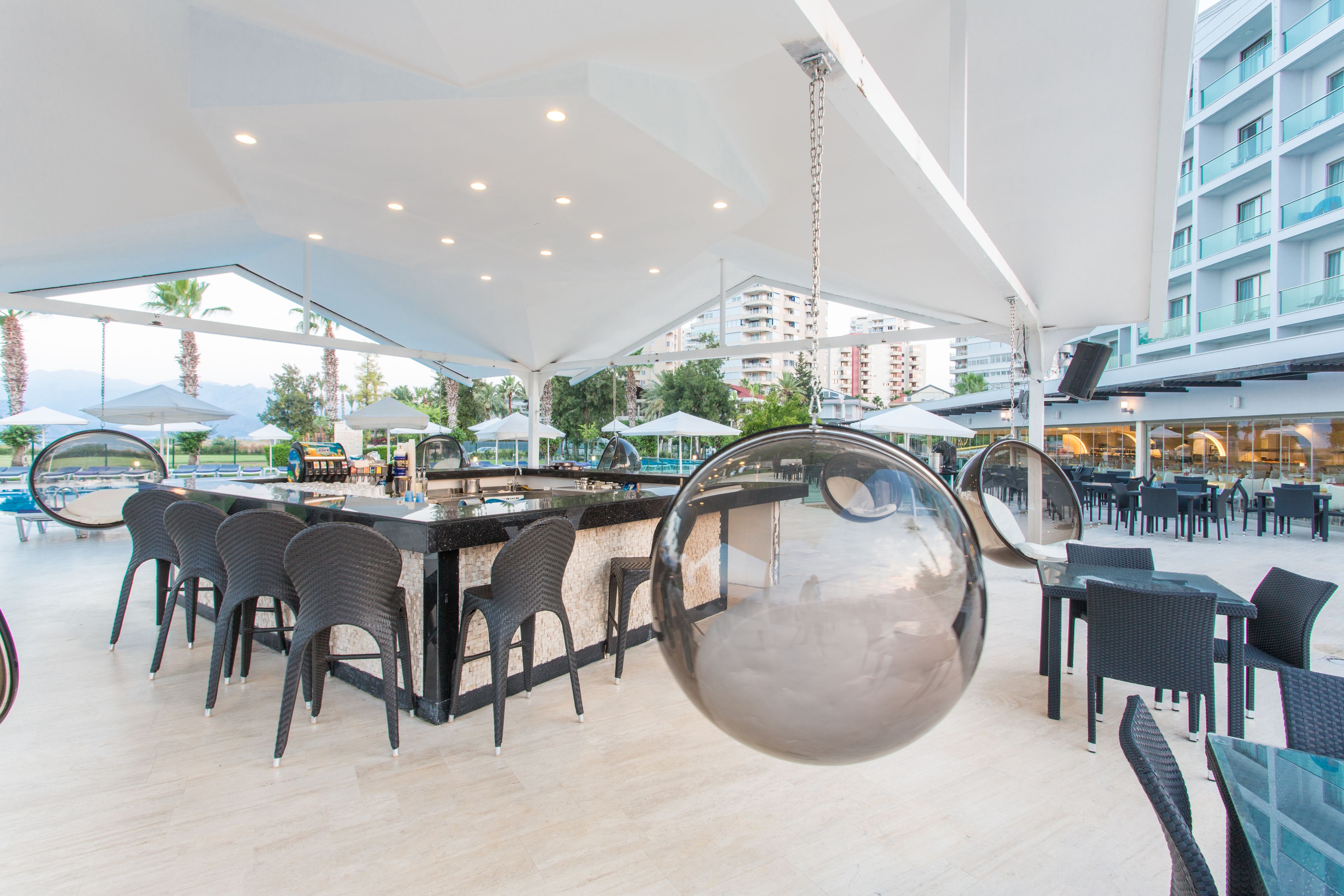 Área de bar ao ar livre com design moderno, apresentando balcão, assentos e grandes esferas refletivas.