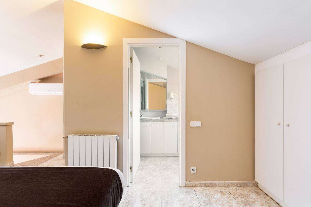 Quarto com cama, radiador, porta para um banheiro e vista para uma praia.