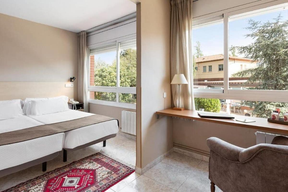 Quarto de hotel com cama, escrivaninha, cadeira e vista para o exterior.