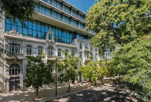 Um edifício de vários andares com fachada clássica, grandes janelas e um pátio com árvores.