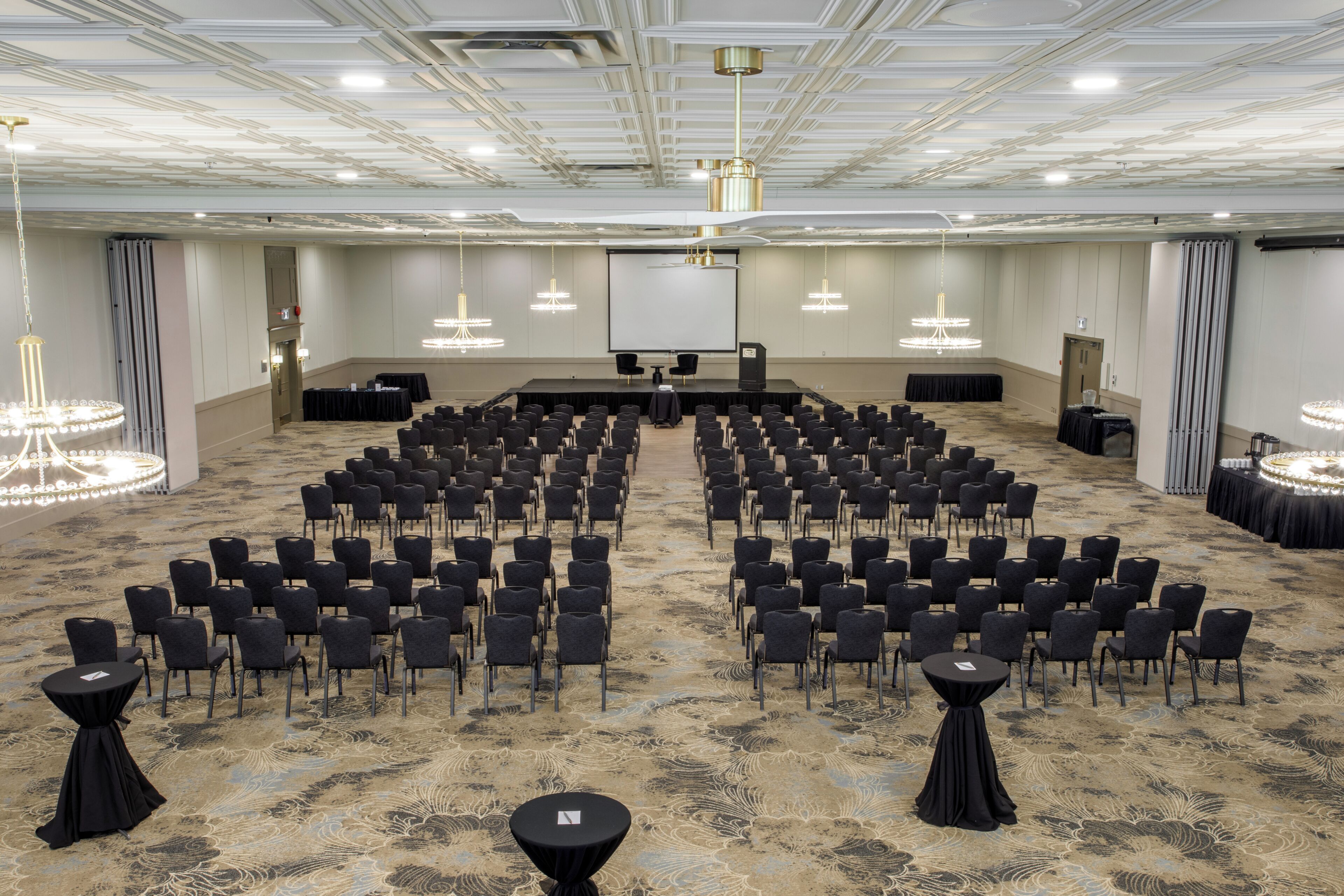 Uma sala de conferências com fileiras de cadeiras, um palco e uma tela grande.