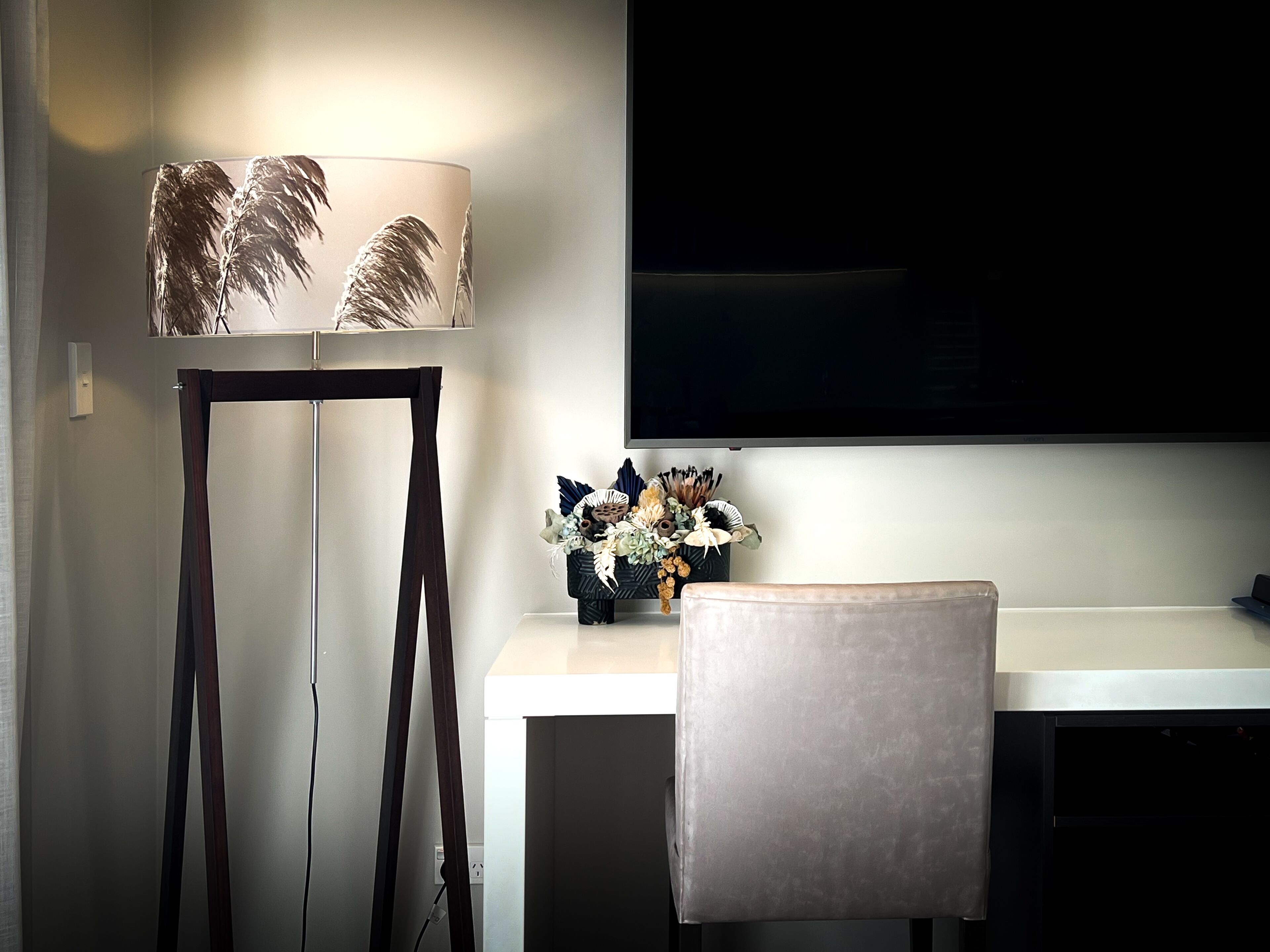 Quarto moderno com escrivaninha, cadeira, abajur com cúpulas de pena e televisão de tela plana na parede.
