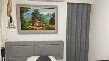 Quarto de hotel com cama, pintura, ar condicionado, telefone e cortina.