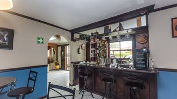 Uma área de bar com banquetas, balcão e diversas garrafas e copos.