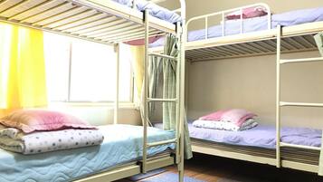 Um dormitório com beliches, uma janela com cortinas e um tapete azul.
