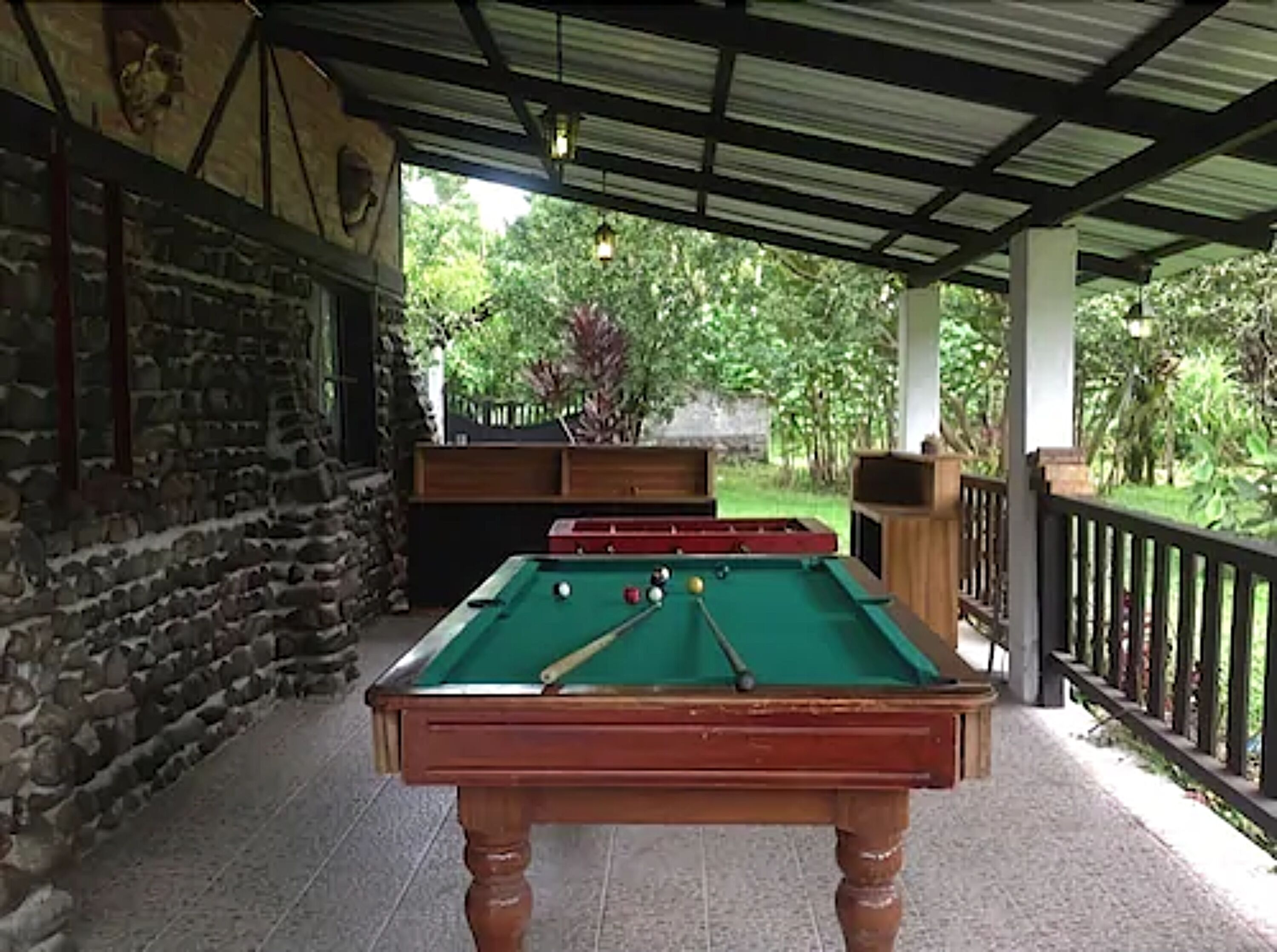 Mesa de bilhar numa área externa coberta, com paredes de pedra e vista para o verde.