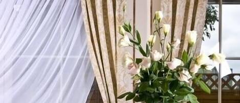 Mesa de jantar posta para seis com toalhas brancas, cadeiras listradas e um vaso de flores brancas.