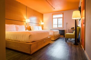 Quarto de hotel moderno com uma cama grande, mesas de cabeceira, uma escrivaninha e uma cadeira.
