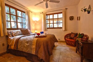 Quarto com cama grande, duas janelas, ventilador de teto e mesa de cabeceira com abajur.
