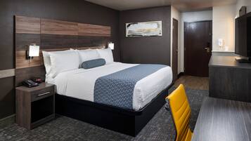 Quarto de hotel com cama, mesa de cabeceira, cadeira e escrivaninha com cadeira.