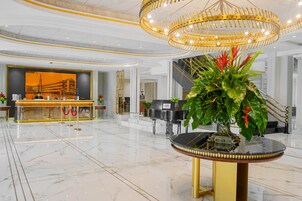 Um hall luxuoso com piso de mármore, balcão de recepção, um lustre imponente e um piano.