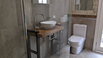 Uma casa de banho moderna com uma grande pia branca, uma sanita e um compartimento de duche com parede de vidro.