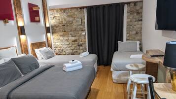 Quarto de hotel com duas camas, parede de pedra, televisão de tela plana e uma pequena mesa com abajur.
