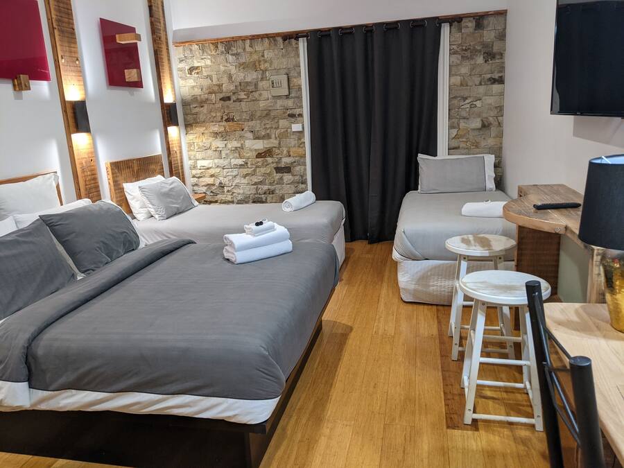 Quarto de hotel com duas camas, parede de pedra, televisão de tela plana e uma pequena mesa com abajur.