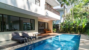 Uma casa moderna com piscina, área de estar externa e vegetação exuberante.