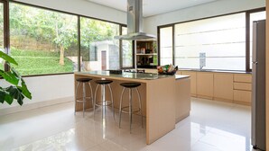 Cozinha moderna com ilha central, banquetas de bar e grandes janelas com vista para o verde.