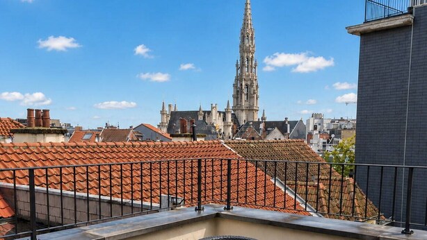 Terraço no telhado com móveis de vime, uma garrafa de champanhe e vista para o campanário de uma igreja histórica.