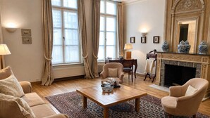 Sala de estar com sofá, poltronas, mesa de centro, lareira e tapete estampado.