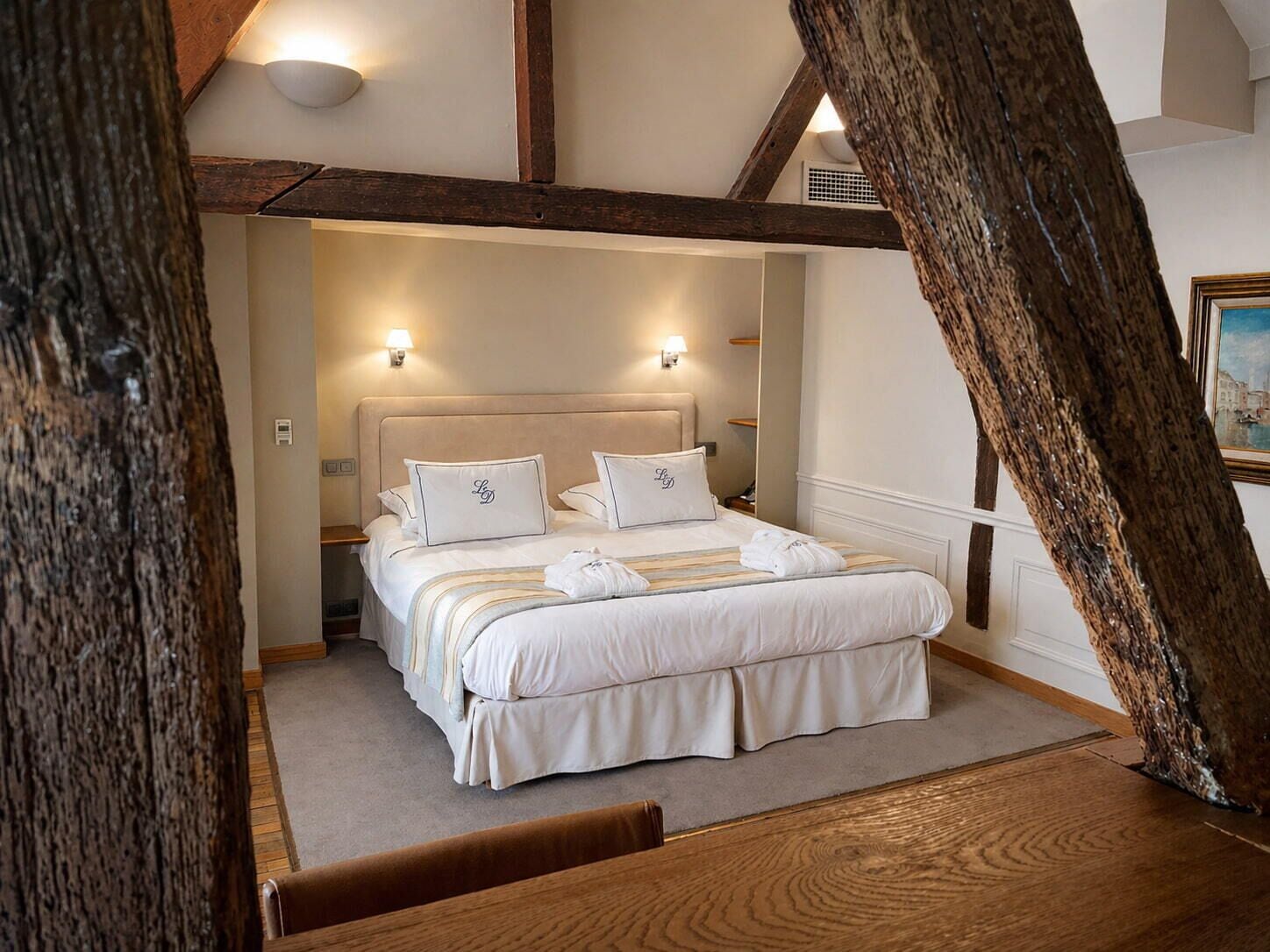Quarto com uma cama grande, duas luminárias de cabeceira e um vigamento de madeira no teto.
