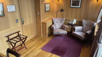 Quarto com painéis de madeira, duas poltronas, um tapete roxo, uma mesinha com copos e um quadro pendurado na parede.