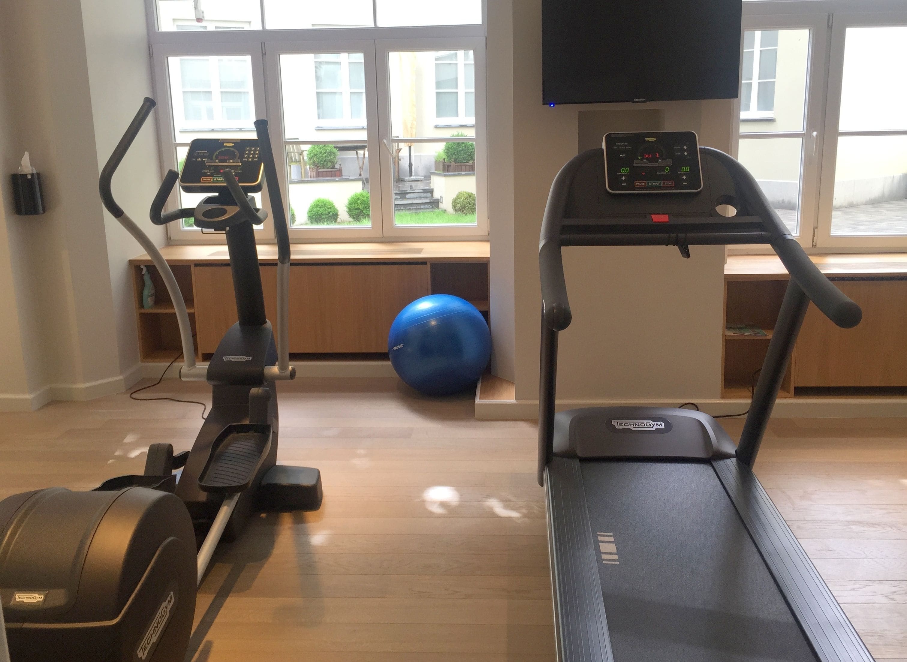 Uma academia com esteiras, elíptico e uma bola de exercícios azul.